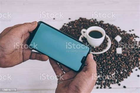 남자는 커피 콩과 테이블에 컵의 배경에 스마트 폰을 들고있다 곡초류에 대한 스톡 사진 및 기타 이미지 곡초류 남자 머그