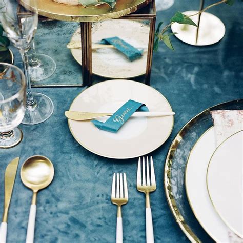 A Table Set With Plates Silverware And Gold Rimmed Utensils Is Seen In