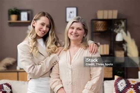아름다운 노인 어머니와 성인 딸이 포옹하고 카메라를보고 아늑한 거실을 배경으로 미소 지으십시오 관계 가족 사랑 부모에 대한 스톡