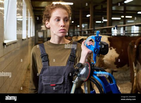 Young Female Farm Worker With Milking Machine In Hand Walking Along
