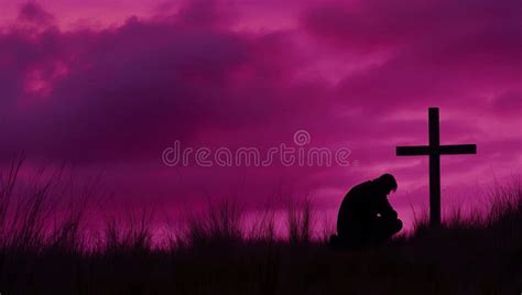 On A Meadow Grass Field At Sunset A Man Prays Beside A Wooden Cross