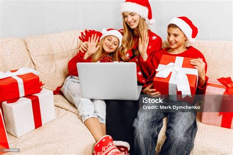 행복한 가족 젊은 어머니와 산타 클로스 모자를 쓴 어린 아이들은 집에서 새해를 축하하고 소파에 앉아 크리스마스 선물을 엽니 다 가상 이벤트에 대한 스톡 사진 및 기타 이미지