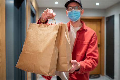 현관에 음식과 종이 봉투를 들고 보호 마스크에 배달 남자 택배는 고객에게 신선한 야채와 과일이있는 상자를 제공합니다 배달에 대한