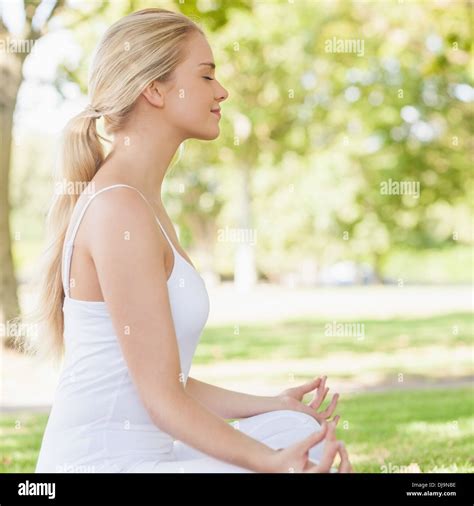 Side View Of Ponytailed Calm Woman Meditating Sitting In A Park Stock