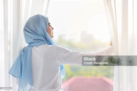 하얀 잠옷을 입고 일출에 아침에 일어난 후 팔을 뻗고 있는 아름다운 아시아 무슬림 여성 파란 히잡을 쓴 귀여운 소녀가 서서 쉬고
