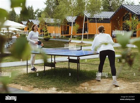 Two Women Engage In Active Game Of Ping Pong At An Outdoor Table Tennis