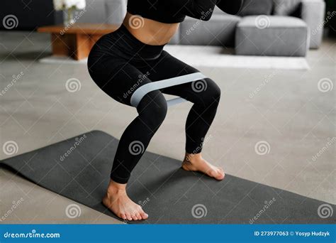 Cute Woman In Sportswear Doing Exercises Squatting On Mat With Rubber Bands On Hips In Living