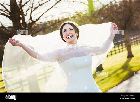 A Bride In Her Wedding Dress Laughing And Holding Her Veil Out Behind