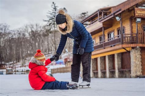 Joven madre enseñando a su pequeño hijo a patinar sobre hielo en la pista de patinaje al aire