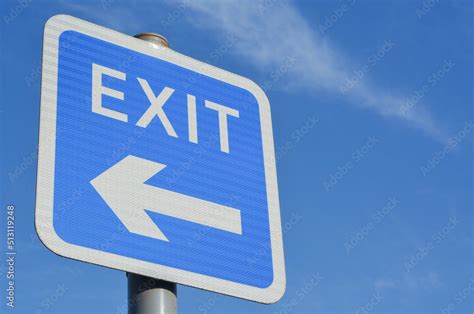 Exit Road Sign With Arrow Symbol Pointing To The Left Against A Clear Blue Sky Stock Photo