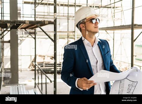 Man Architect Wearing Formal Suit And Hard Hat During Building Construction Control Holding A