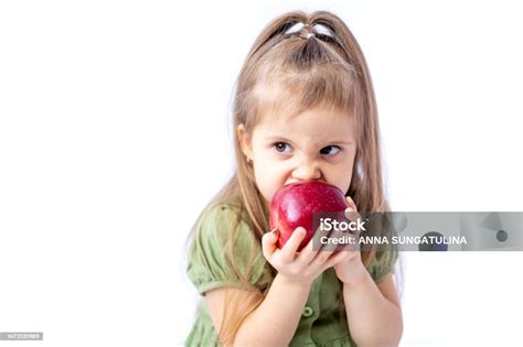 녹색 드레스에 큰 빨간 사과를 먹거나 물어뜯는 귀여운 아기 소녀 흰색 고립 된 배경입니다 어린이를위한 건강 식품 또는 건강한 간식 텍스트를 위한 공간입니다 고품질 사진 2