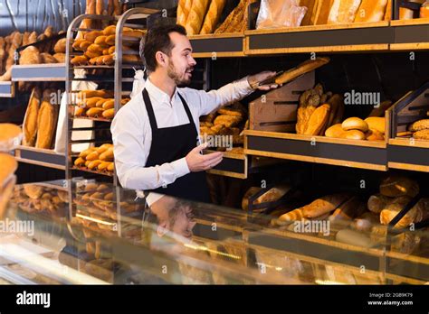 Male Shop Assistant Demonstrating Delicious Loaves Of Bread In Bakery