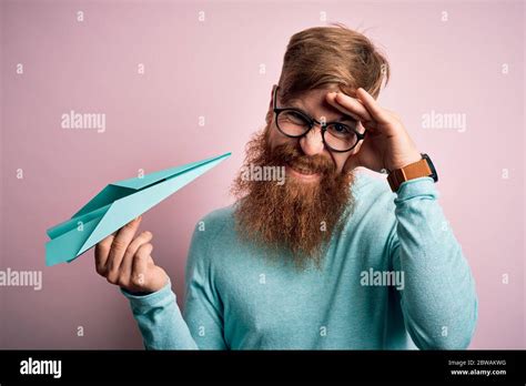 Irish Redhead Man With Beard Holding Paper Plane Over Pink Isolated