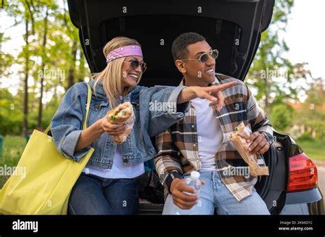 Blonde Woman And African American Man Eating Sandwiches And Looking