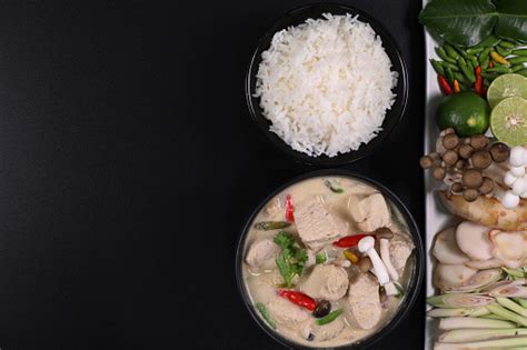 톰 카 가이 태국 치킨 코코넛 수프는 그릇에 담겨 있고 짙은 검은 색 배경에 고립 된 그릇에 쌀이 담겨 있습니다 위쪽 보기에는