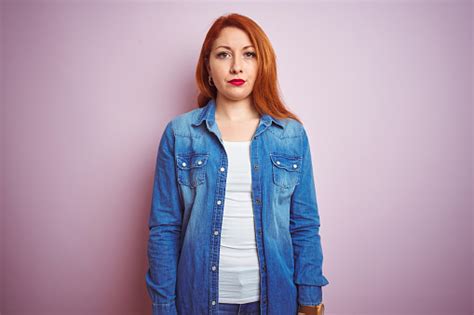 Youg 아름 다운 빨간 머리 여자 데님 셔츠 위에 서 고립 된 분홍색 배경 얼굴에 심각한 표정으로 편안 하 게 카메라를 보는