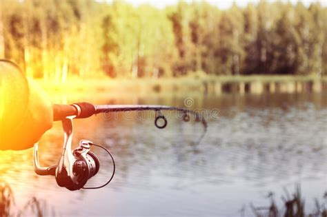 A Fisherman With Fishing Rods A Spinning Reel On The River Bank The
