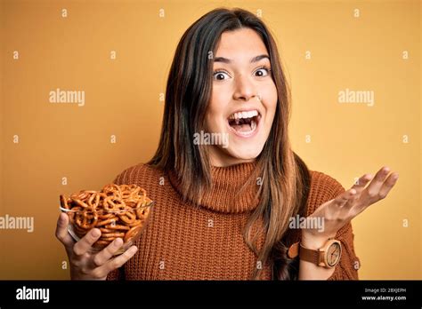 Young Beautiful Girl Eating Baked German Pretzel Standing Over Isolated
