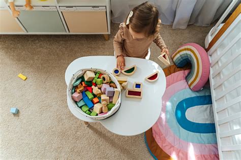 놀이방의 테이블에 나무 블록을 가지고 노는 어린 소녀 현대 보육원에서 아기와 유아를위한 교육 게임 아이는 나무 무지개 쌓기 블록으로 타워를 만듭니다 2 3 살에 대한 스톡