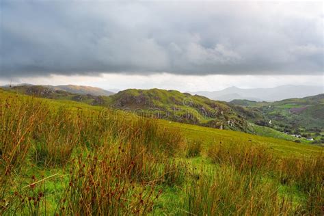 Grassy Fields In The Foreground Lead To Green Rocky Hills Under A