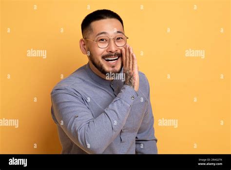 Asian Man Holding Hand Near Mouth Sharing News Or Gossips At Camera