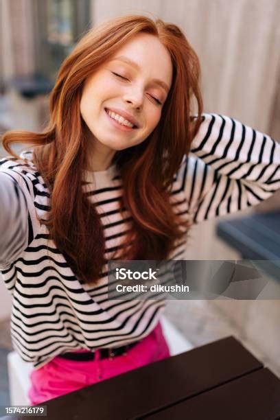 눈을 감고 웃고 있는 여자의 세로 Pov 초상화는 카페의 테이블에 앉아 스마트폰으로 자화상을 찍고 있다 셀카를 찍는 여성의 관점