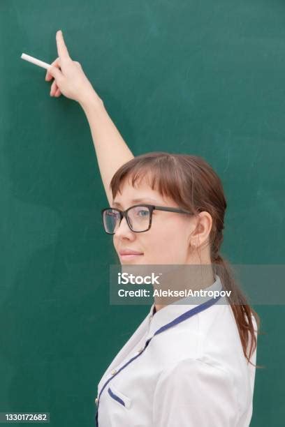 녹색 칠판의 배경에 교실에서 그녀의 손에 분필흰색 블라우스와 안경을 입고 학교 교사 젊은 예쁜 여자 30 34세에 대한 스톡