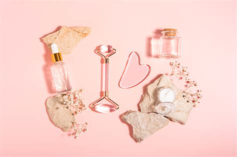 핑크 석영 스톤 롤러 얼굴 마사지기 구아슈 파스텔 핑크 배경에 유리 화장품 병과 흰색 꽃 홈 스파 케어 아름다움과 젊음 안티 에이지의 개념 상단 보기 플랫 레이 0명에 대한