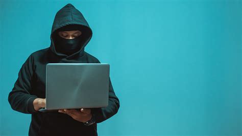 검은 후드 티를 입고 얼굴을 가리고 어두운 배경에서 빛이 위에서 내려 오는 노트북을 들고 얼굴을 가리고 금융 데이터 도난 개념 텍스트를위한 빈 공간 복사 공간 30 34세에