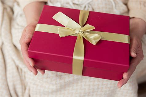 빨간색 선물 상자는 여성의 무릎에 들고 금색 리본으로 아름답게 싸여 있습니다 어머니의 날 생일 행사 가정의 방에 대한 스톡 사진