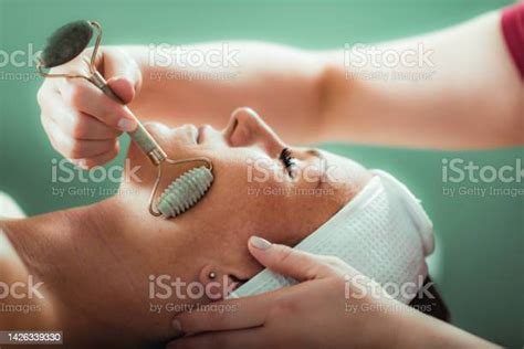 뷰티 살롱의 Guasha 얼굴 마사지 비취 돌 롤러를 사용하여 얼굴의 압력 포인트를 자극하는 마사지 기술 얼굴 마사지에 대한