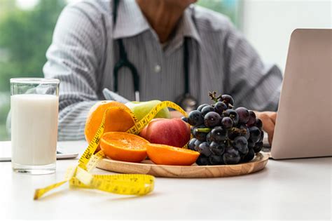 병원 사무실의 테이블에 건강 한 음식 과일과 우유와 함께 책상에서 일 하는 수석 남성 영양사 의사 다이어트와 잘 먹고 메뉴