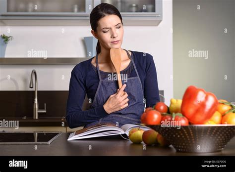 Serious Pretty Woman Wearing Apron Holding Wooden Ladle While Reading A