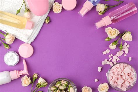 밝은 보라색 배경에 신선한 장미와 분홍색 병에 얼굴과 몸에 대한 화장품 크림과 로션 바다 소금과 비누 스파 위에서 볼 수