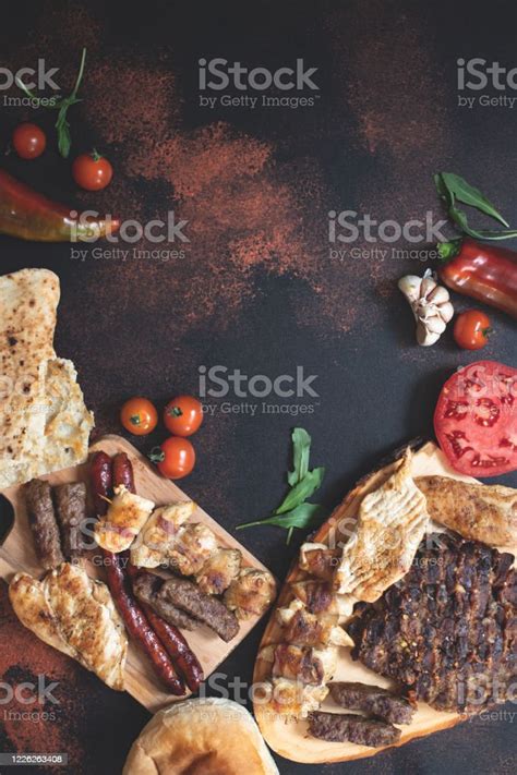 어두운 소박한 배경에 신선한 야채와 빵나무 도마에 제공되는 다양한 구운 고기 전통적인 세르비아어와 발칸 바베큐 고기 로스틸리라는