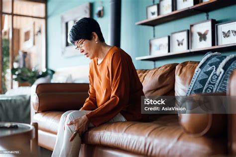 산만 한 선임 아시아 여성은 기분이 좋지 않고 집에서 거실에있는 소파에 앉아있는 동안 다리에 통증으로 고통 아픔에 대한 스톡