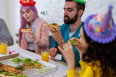 네 명의 현대 젊은 친구들이 식사와 음료와 함께 생일 저녁을 축하하고 있습니다 피자 타임입니다 25 29세에 대한 스톡 사진 및