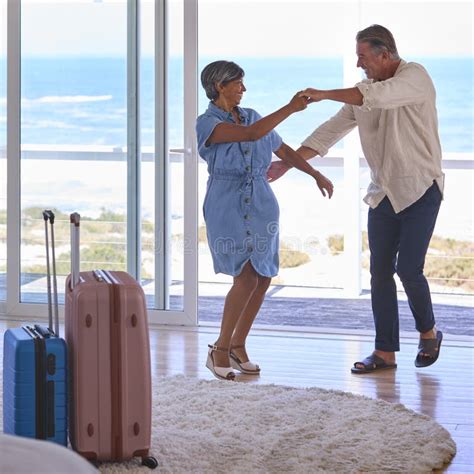 Mature Couple With Luggage Dancing In Beachfront House Overlooking