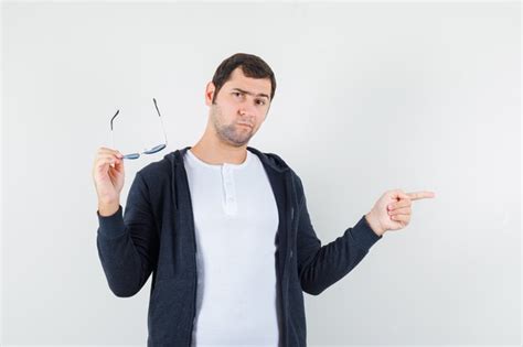T 셔츠 재킷 들고 안경 옆으로 가리키고 주저 전면보기에 젊은 남성 무료 사진