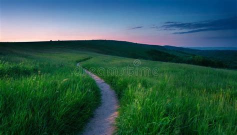 Picturesque Winding Path Through A Green Grass Field In Hilly Area At