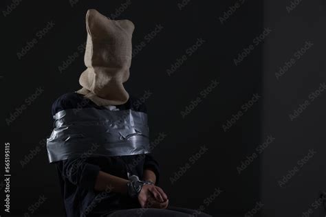 Taped Up Woman With Bag On Her Head On Dark Background Space For Text Hostage Stock Photo
