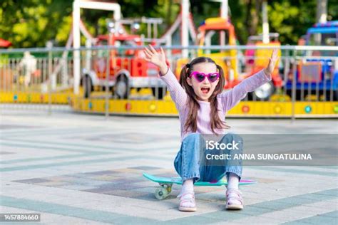 놀이 공원에서 어린 소녀는 여름에 스케이트 보드를 타고 선글라스 여름 휴가 및 방학의 개념에 회전 목마 근처에서 행복과 함께 미소 2 3 살에 대한 스톡 사진 및 기타