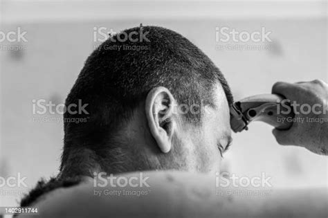 중년 남성이 머리를 자른다 그 사람은 전기 머리 깎기로 머리에 머리카락을 자릅니다 짧은 갈색 머리 거실 내부 선택적 초점 흑백