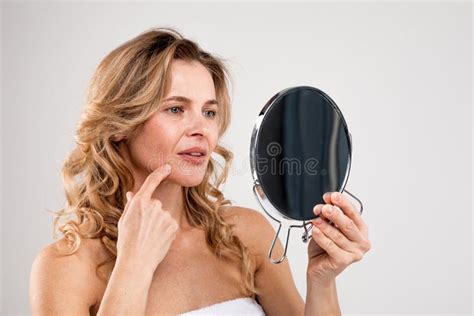 Frustrated Middle Aged Lady Holding Mirror And Looking At Pimple On