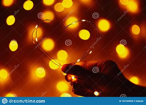 Woman Hand Holding Wire In A Shape Of Heart Against Abstract Background