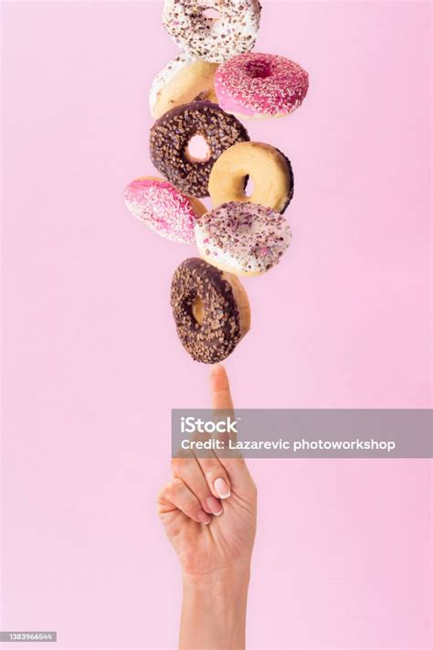 분홍색 파스텔 배경에 흰색 초콜릿 분홍색 유약과 다채로운 부스러기가있는 아름다운 여성의 손이 떨어지는 링 도넛 도넛에 대한 스톡 사진 및 기타 이미지 Istock