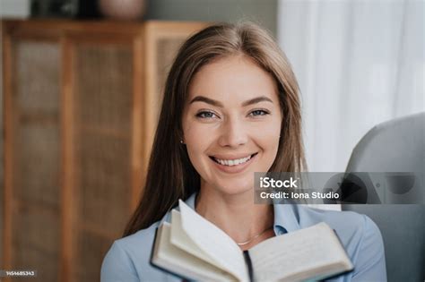 파란 셔츠를 입은 쾌활한 백인 여성이 일기를 열고 집에서 카메라 이빨 미소를 짓고 있습니다 사랑스러운 이탈리아 소녀는 책을 제공합니다 예쁜 금발 여성 계획 주간 성공한