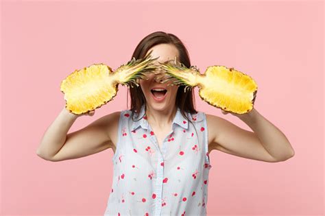 분홍색 파스텔 벽 배경에 고립 된 신선한 잘 익은 파인애플 과일의 Halfs와 눈을 덮고 있는 여름 옷을 들고 젊은 여자