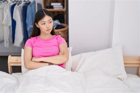 Chinese Woman Sitting On Bed With Arms Crossed Gesture And Serious